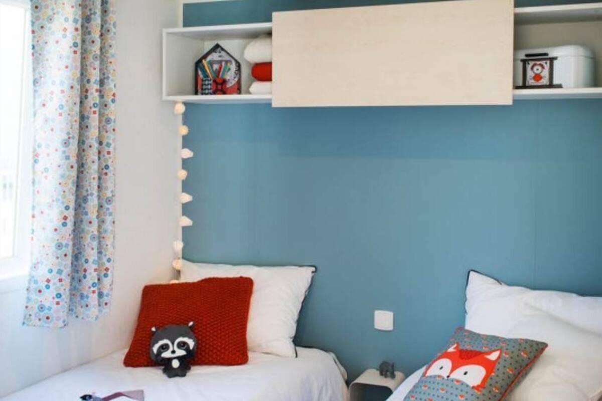 Quarto com duas camas, uma estante acima e uma janela com cortinas.