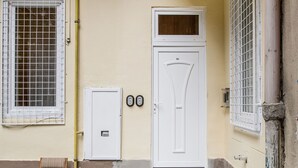 Entrada de um edifício com porta branca, uma pequena janela com grade de metal e uma cadeira do lado de fora.