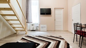 Quarto com escada de madeira, televisão de tela plana na parede, uma porta e uma cadeira com almofada vermelha.