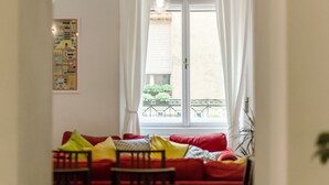Uma sala de jantar com um sofá vermelho, uma mesa e uma janela com cortinas brancas.