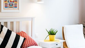 Quarto de hotel bem arrumado com uma cama, uma cadeira, uma mesa de cabeceira com abajur e uma obra de arte emoldurada na parede.