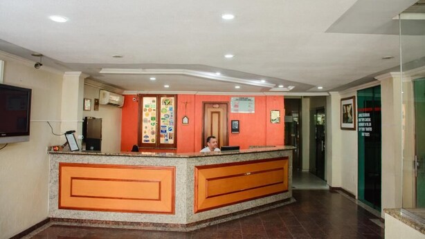 Uma área de recepção com balcão de mármore, televisão e um quadro de informações fixado na parede.
