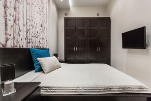 Quarto com cama, mesa de cabeceira, abajur, televisão e guarda-roupa.