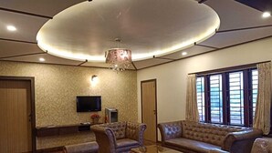 Uma sala de estar ampla com um sofá grande, duas poltronas, uma mesa de centro e uma televisão na parede.