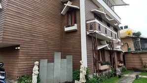 Um edifício moderno com fachada de madeira, uma varanda e um jardim com estátuas.