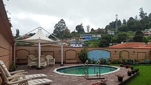 Uma área de piscina externa com espreguiçadeiras, um espaço de estar coberto e uma parede em mosaico.