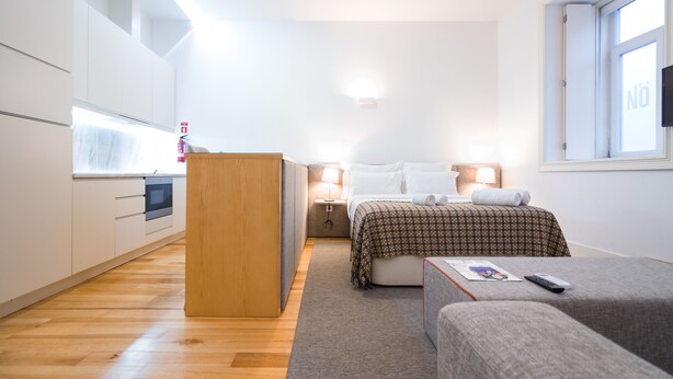Quarto de hotel pequeno com cozinha compacta, cama com colcha estampada, abajures e janela com vista.