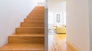 Uma escada de madeira leva a uma sala de estar com um sofá e uma mesinha.