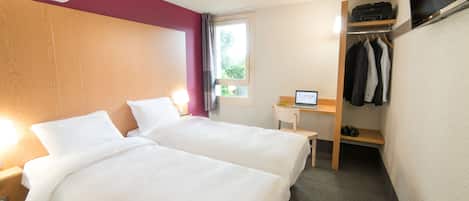 Quarto de hotel com duas camas, uma escrivaninha, uma cadeira, um guarda-roupa e uma janela.