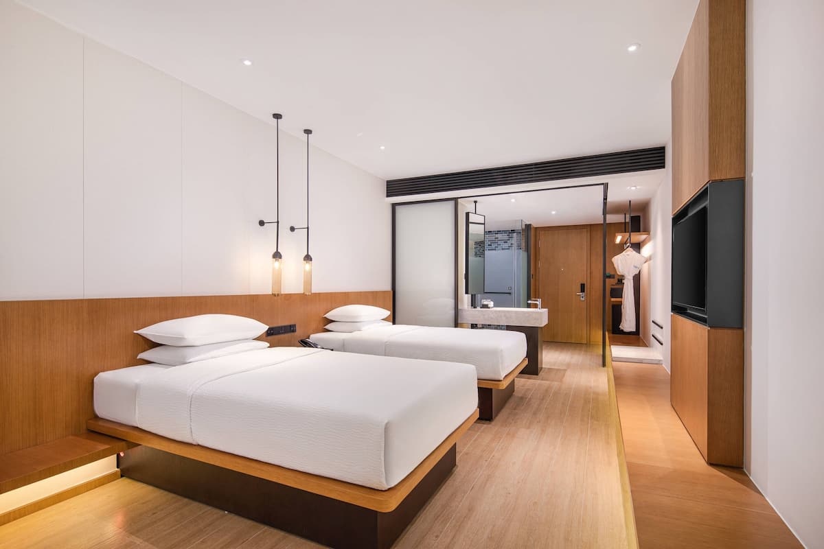 Quarto de hotel moderno com duas camas, um espelho grande, uma TV e banheiro com pia e espelho.