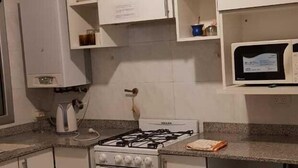 Cozinha com armários brancos, fogão a gás, micro-ondas e lixeira.