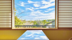 Quarto com uma grande janela que oferece vista para uma paisagem arborizada e um edifício ao longe.