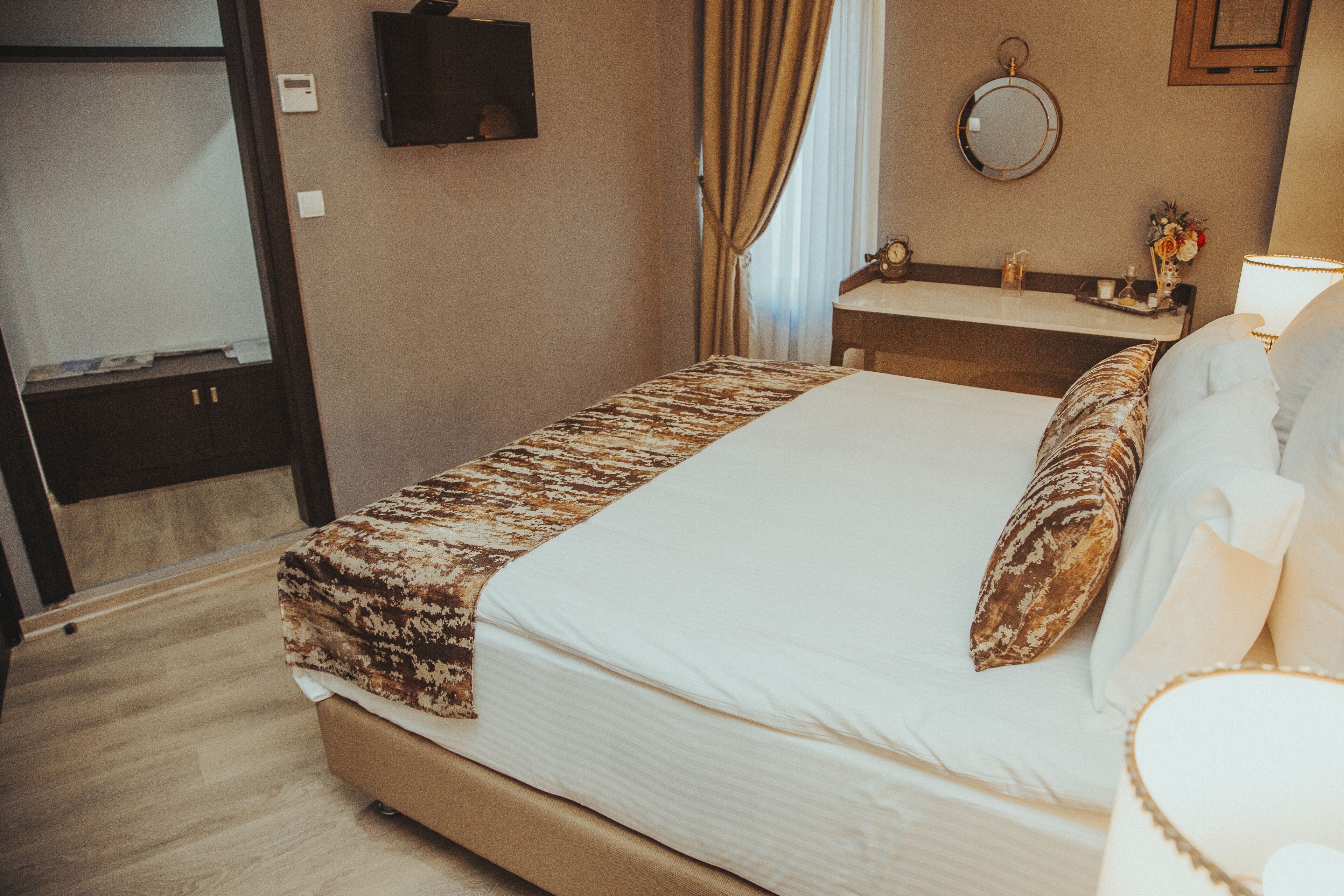 Quarto de hotel com cama, mesa de cabeceira, espelho, janela com cortinas e banheiro com pia e espelho.