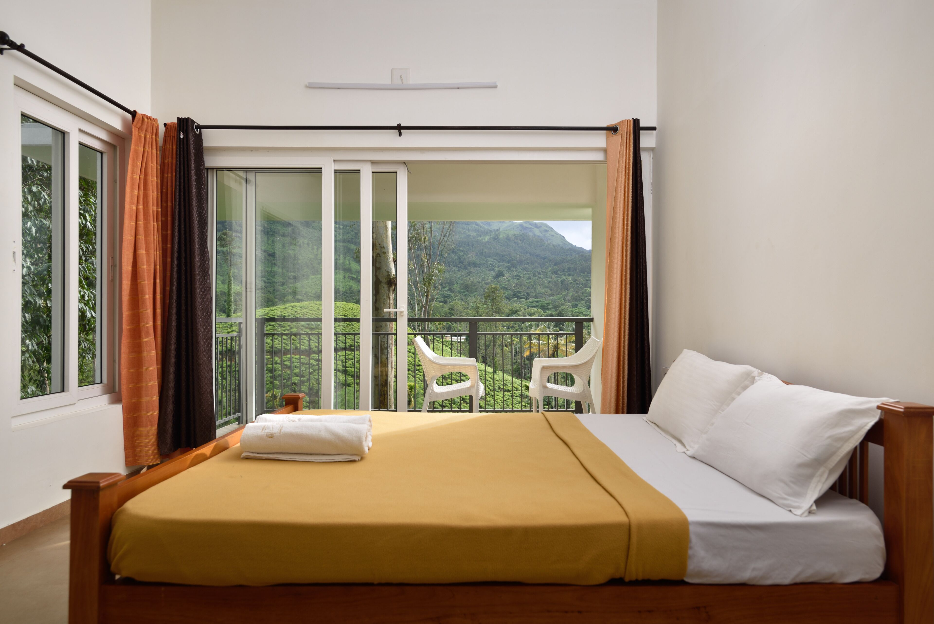 Quarto de hotel com cama, varanda com cadeiras e vista para uma paisagem montanhosa.