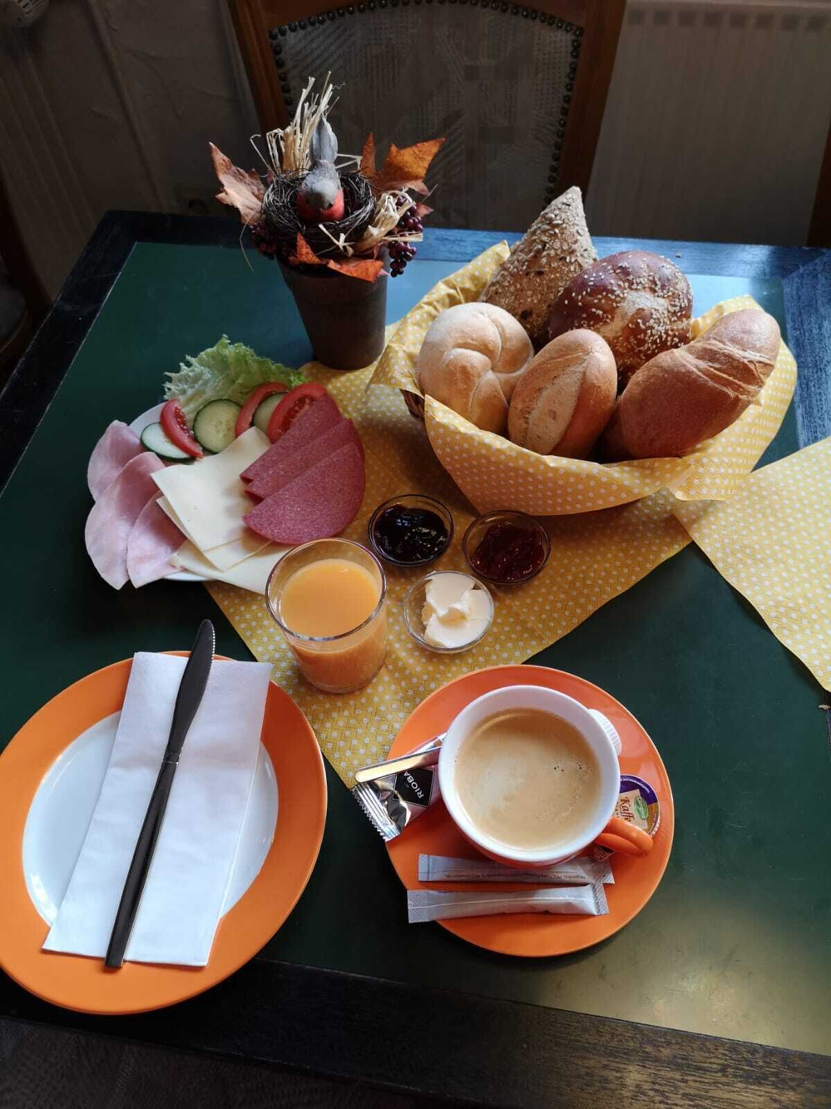 Uma mesa posta para o café da manhã, com pão, presunto, queijo e frutas.