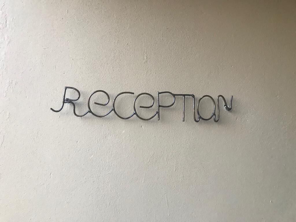 Placa de metal com a palavra 'Reception' numa parede lisa.
