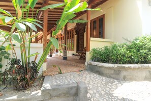Um espaço ao ar livre coberto, com piso de pedra, colunas de madeira e plantas em vasos.