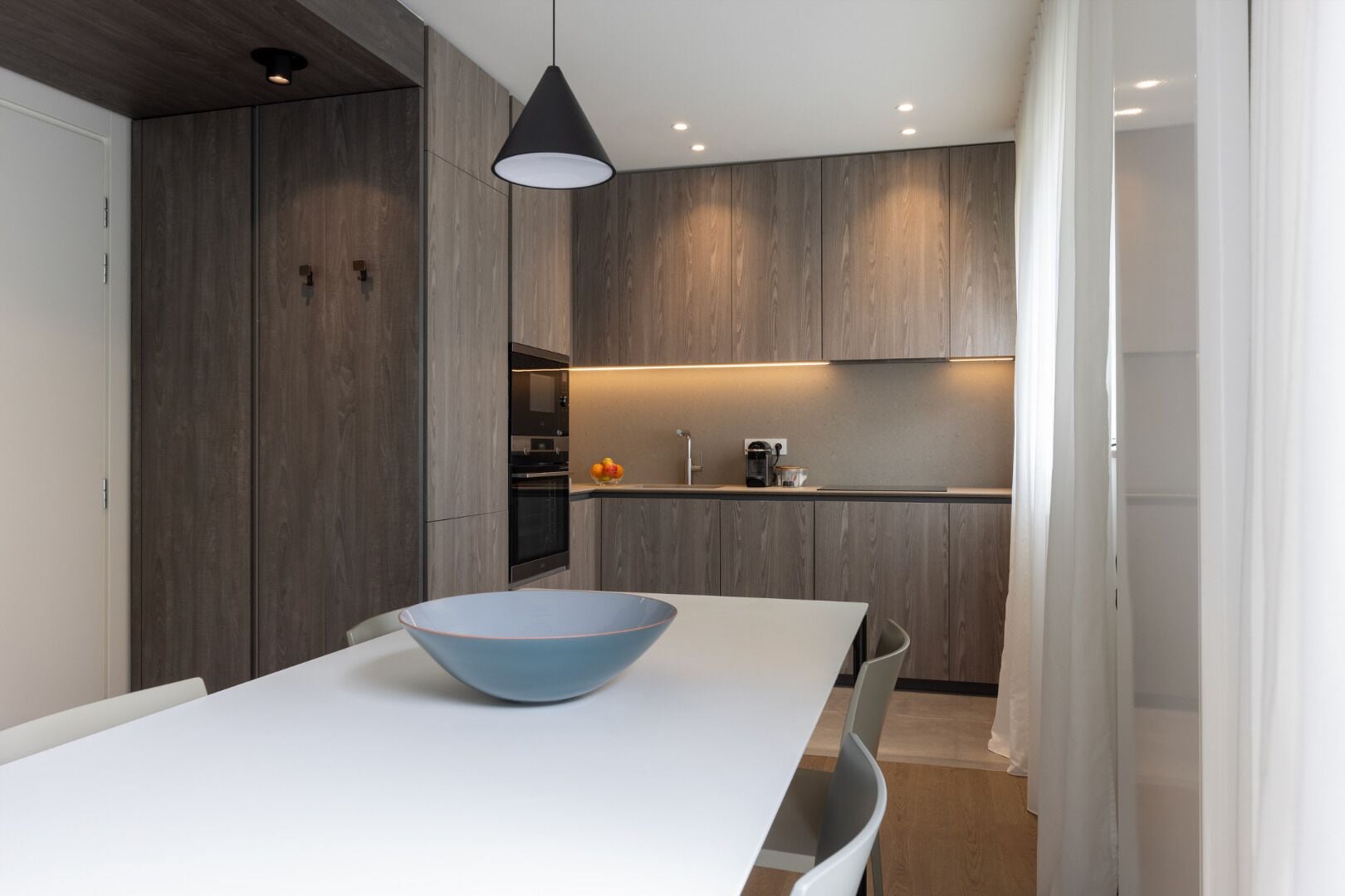 Cozinha moderna com armários de madeira, bancada branca e uma tigela azul na mesa.