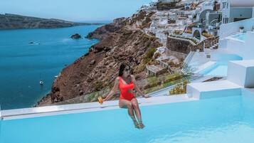 Mulher sentada na borda da piscina com vista para uma cidade costeira e o mar.