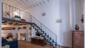 Uma sala de estar ampla com piso de madeira, um sofá azul, um armário de madeira e uma escada com grades de vidro.