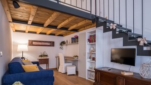 Uma sala de estar moderna com um sofá azul, vigas de madeira no teto, uma televisão e uma escada decorada com laços.