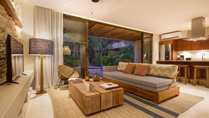 Sala de estar moderna com sofá, mesa de centro e vista para um jardim através de grandes janelas.