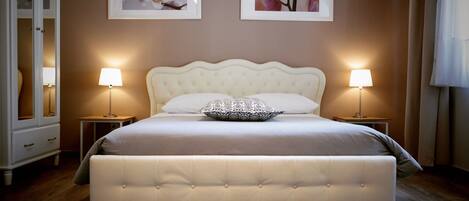 Quarto com uma cama grande, duas mesas de cabeceira com abajures, um guarda-roupa e duas imagens emolduradas na parede.