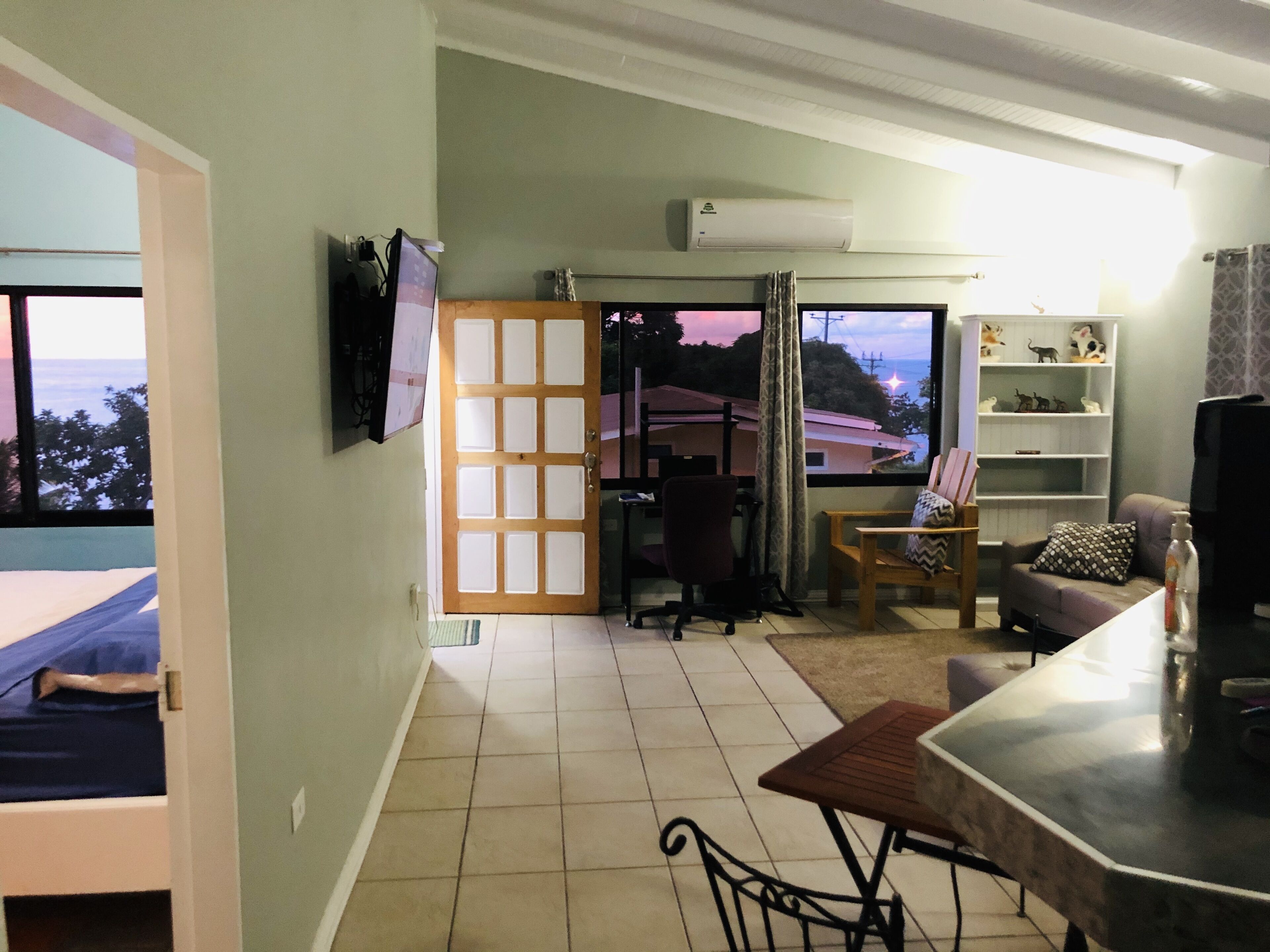 Sala de estar com televisão, sofá, mesa de centro e vista para o exterior.