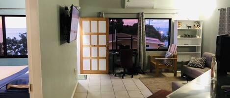 Sala de estar com televisão, sofá, mesa de centro e vista para o exterior.