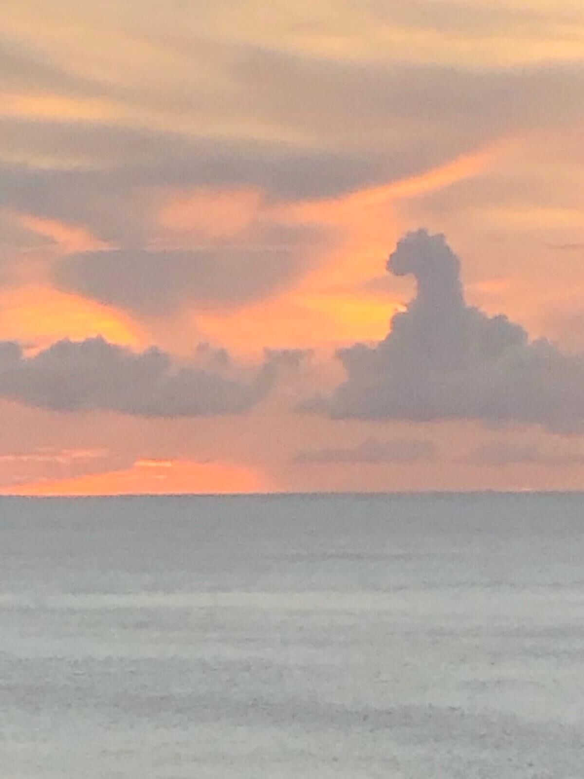 Um pôr do sol sobre um mar calmo, com nuvens no céu.