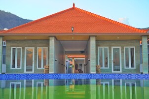 Um edifício com telhado de telhas vermelhas, piscina em frente e vista para as montanhas ao fundo.