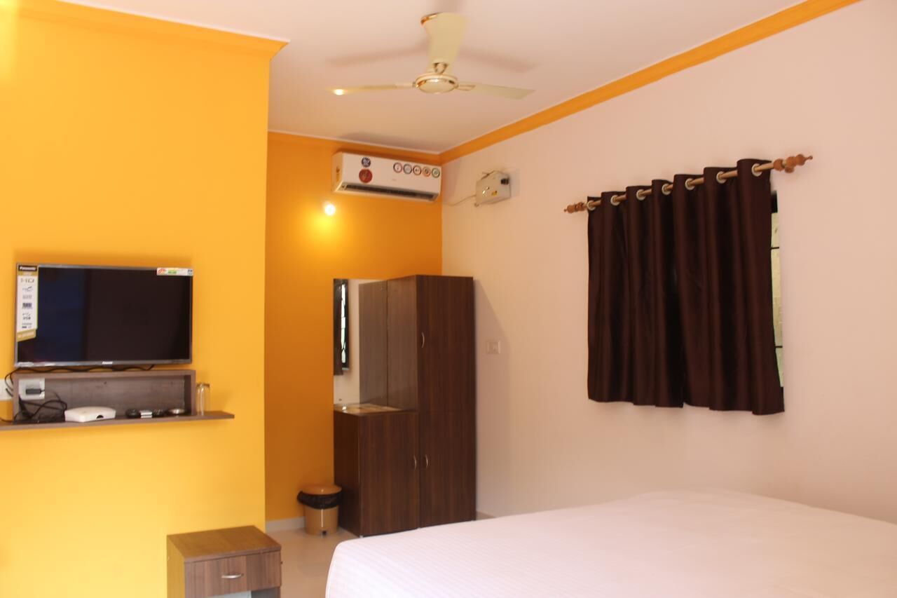 Quarto de hotel com cama, guarda-roupa, televisão, ar condicionado e ventoinha de teto.