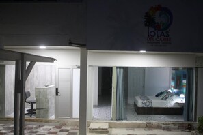 Quarto de hotel com uma cama, uma escrivaninha e uma cadeira. Tem uma janela com cortinas e vista para o exterior.