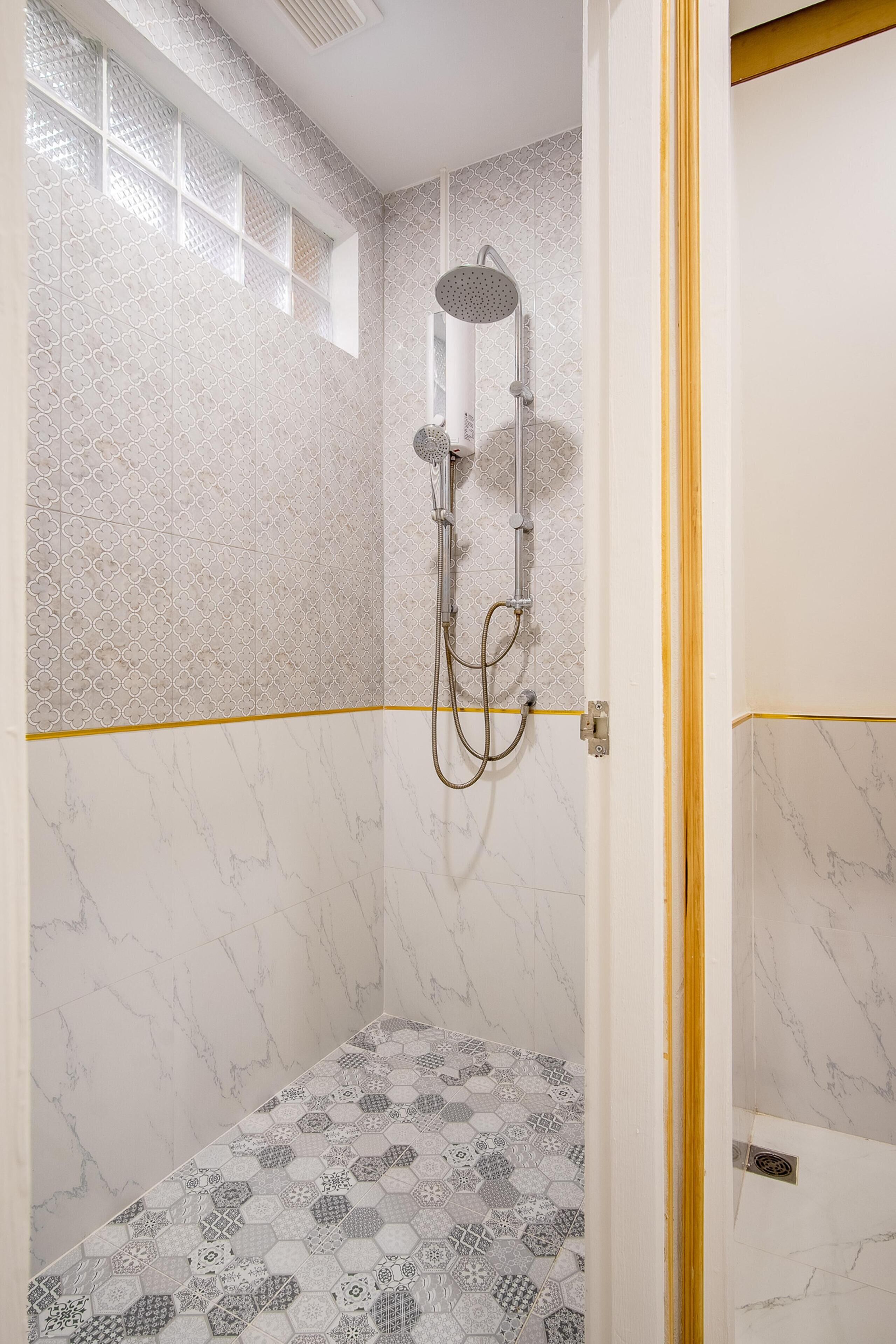 Chuveiro com padrão geométrico de azulejos nas paredes e no chão, um chuveiro manual e uma torneira fixada na parede.