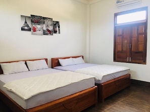 Quarto com duas camas de madeira, roupa de cama branca e ar condicionado fixado na parede.