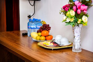 Uma mesa de madeira com uma fruteira, garrafas de água, um vaso com flores e uma bandeja com chávenas e embalagem.