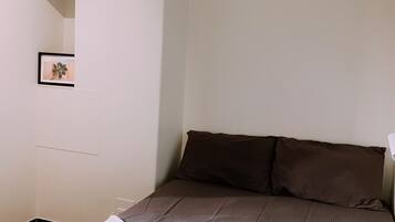 Um quarto com uma cama, travesseiros, um cobertor e uma moldura com uma imagem na parede.