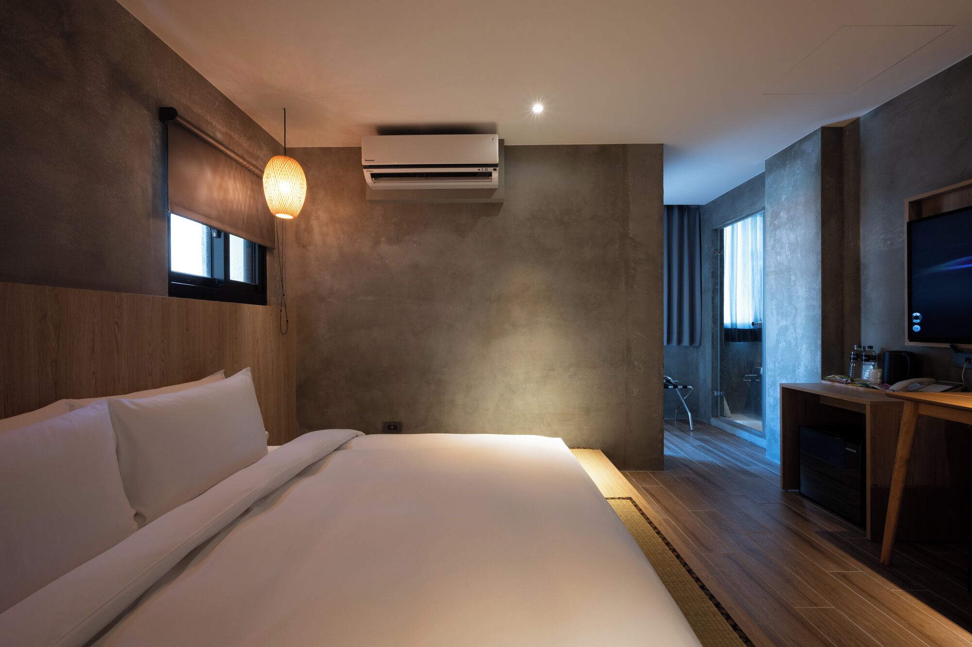 Quarto de hotel moderno com uma cama grande, um ar condicionado, uma mesa com um computador e uma televisão.