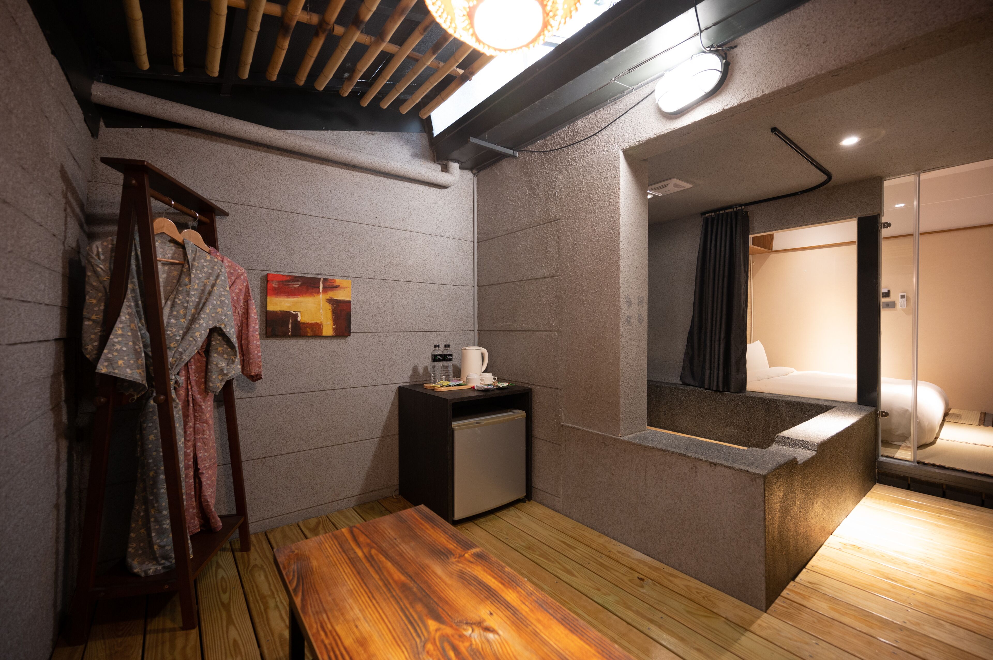 Quarto pequeno e moderno com mesa de madeira, mini-frigorífico, espelho e chuveiro.