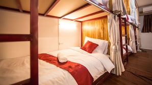 Quarto com beliche, vigas de madeira, roupa de cama branca e travesseiro vermelho.