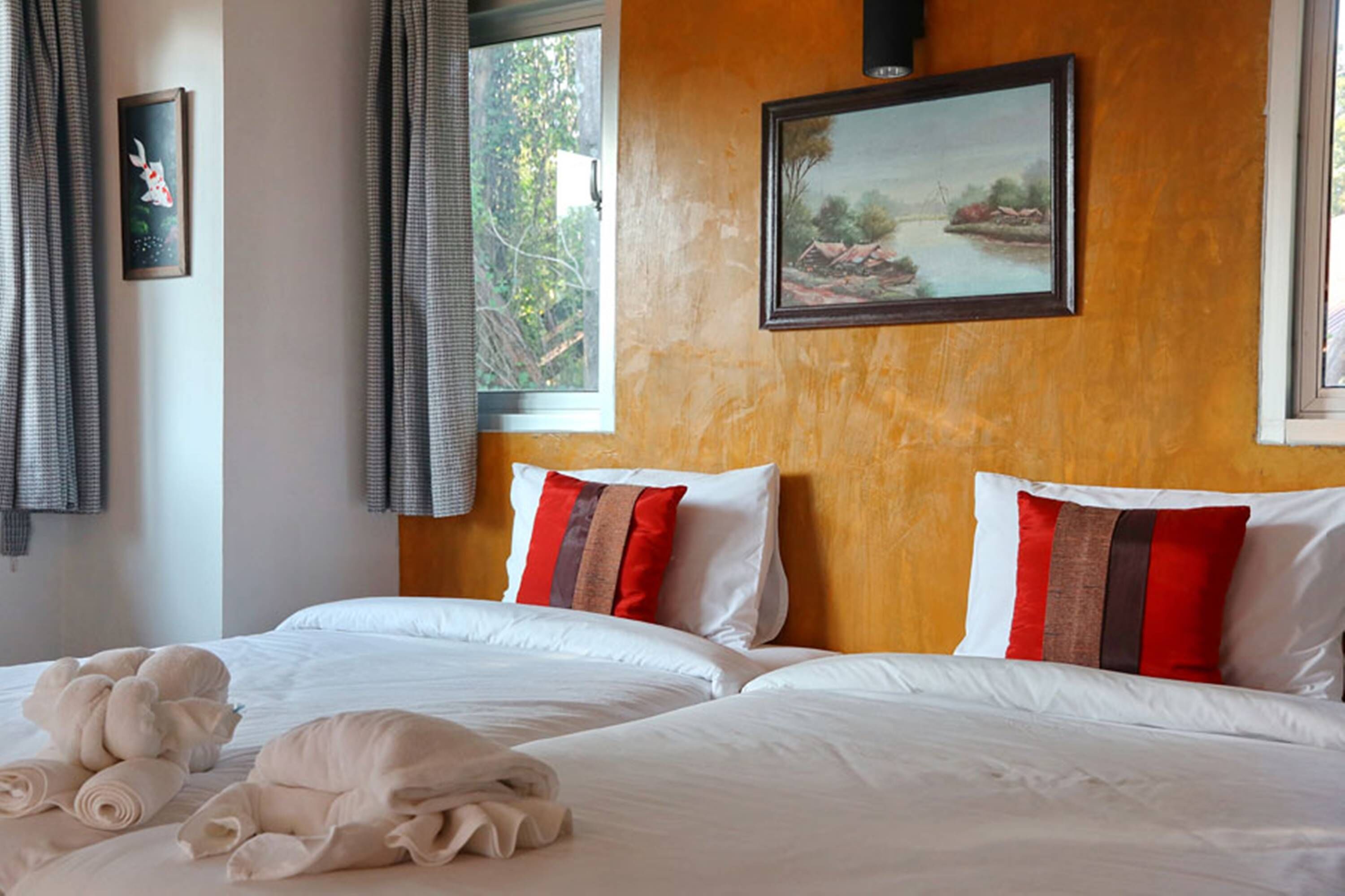 Quarto de hotel com duas camas, um quadro na parede e uma janela com cortinas.