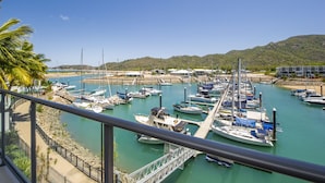 Marina com barcos atracados, céu claro e montanhas ao fundo.