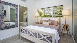 Quarto com cama, espelho grande, janela com persianas e mesa de cabeceira com abajur.