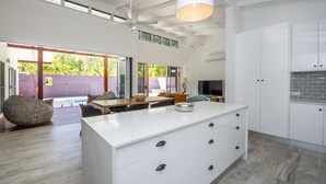 Uma cozinha moderna com armários brancos, uma ilha grande com gavetas e uma área de refeições com mesa e cadeiras de madeira.