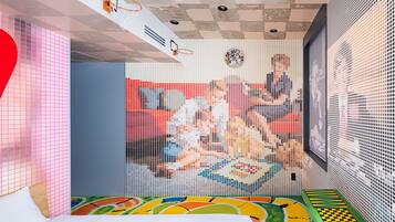 Um quarto com uma cama, um tapete colorido, uma parede com obra de arte em mosaico e um aro de basquete.