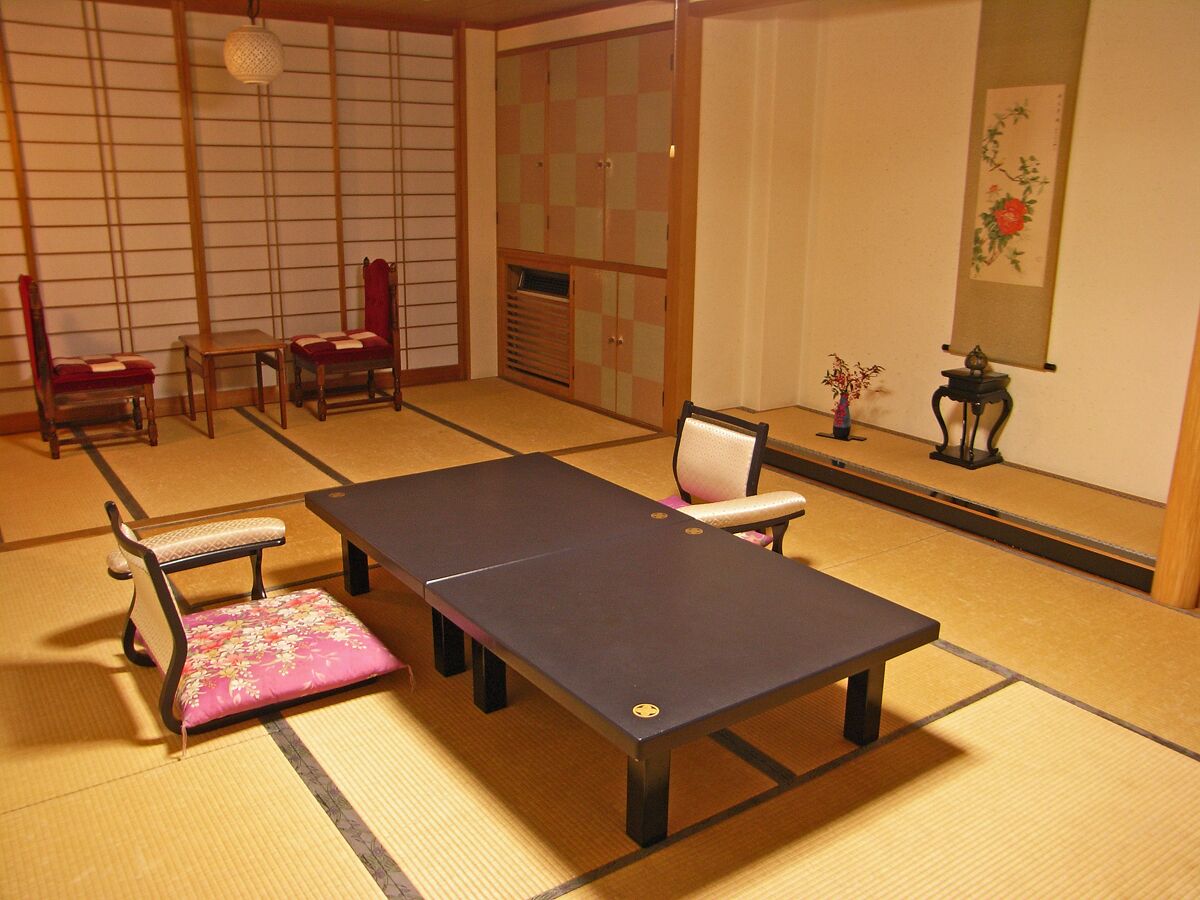 Um espaço com tatames, incluindo uma mesa e duas cadeiras de tatame, um armário de madeira e um painel shoji.