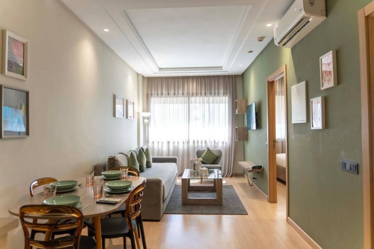 Uma sala de estar moderna com área de jantar, sofá, mesa de centro e televisão na parede.