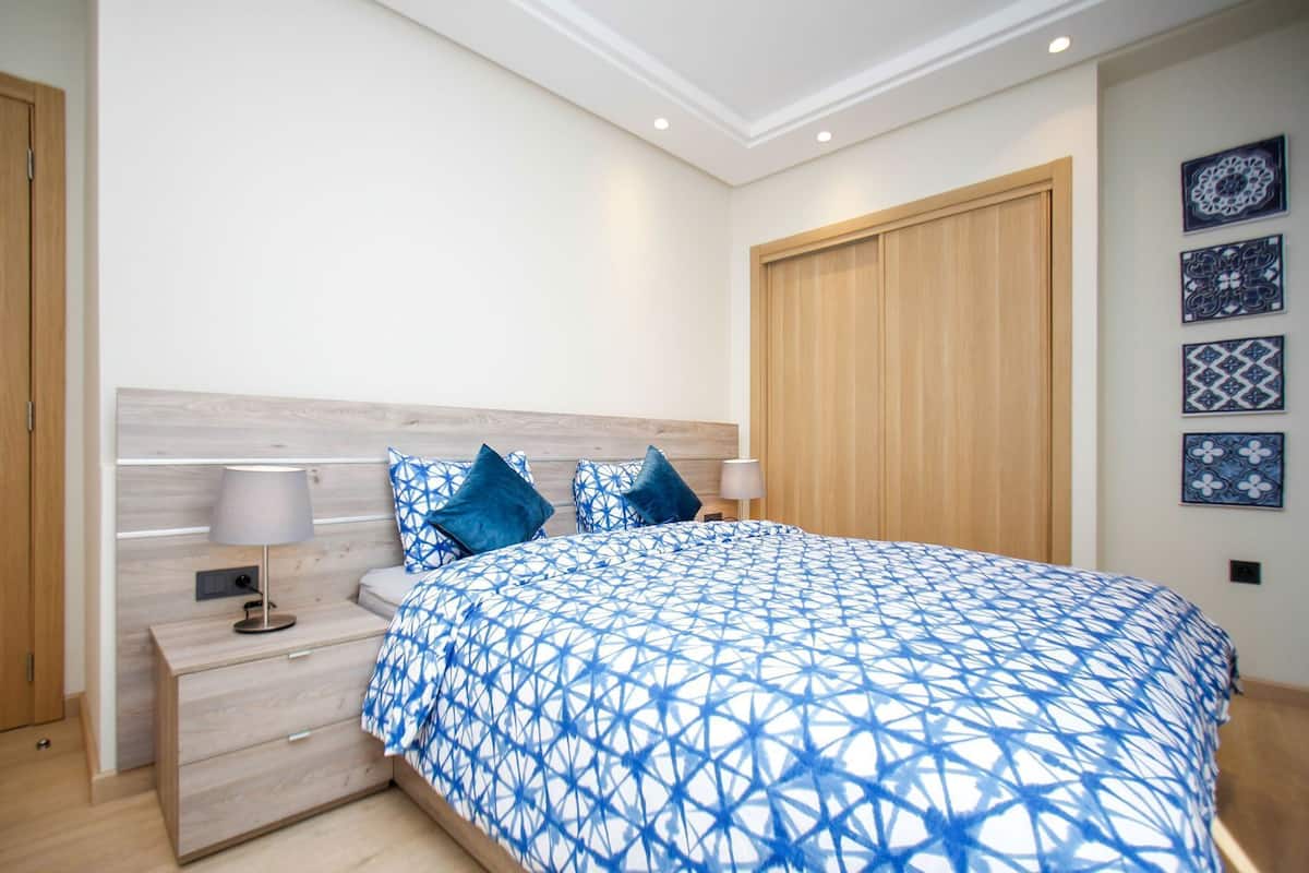 Quarto com cama, mesas de cabeceira, guarda-roupa de madeira e azulejos decorativos.