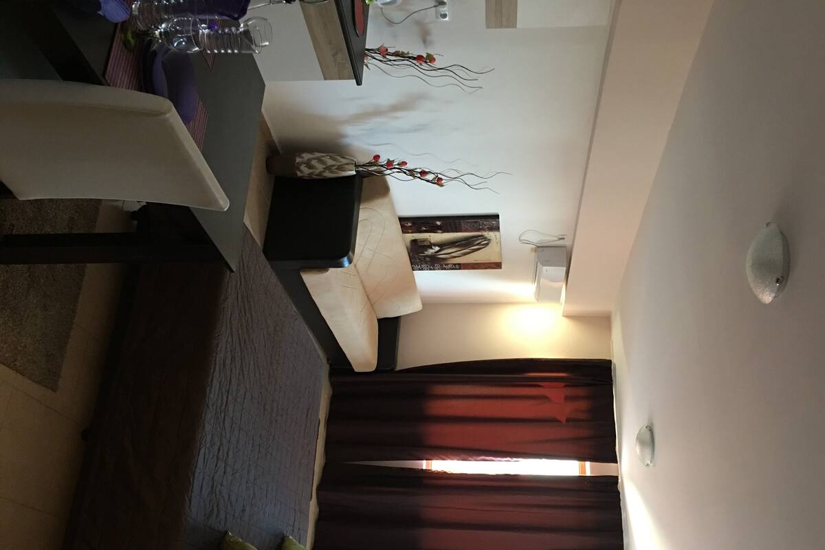 Uma sala de estar com sofá, mesa de centro, televisão e janela com cortinas.
