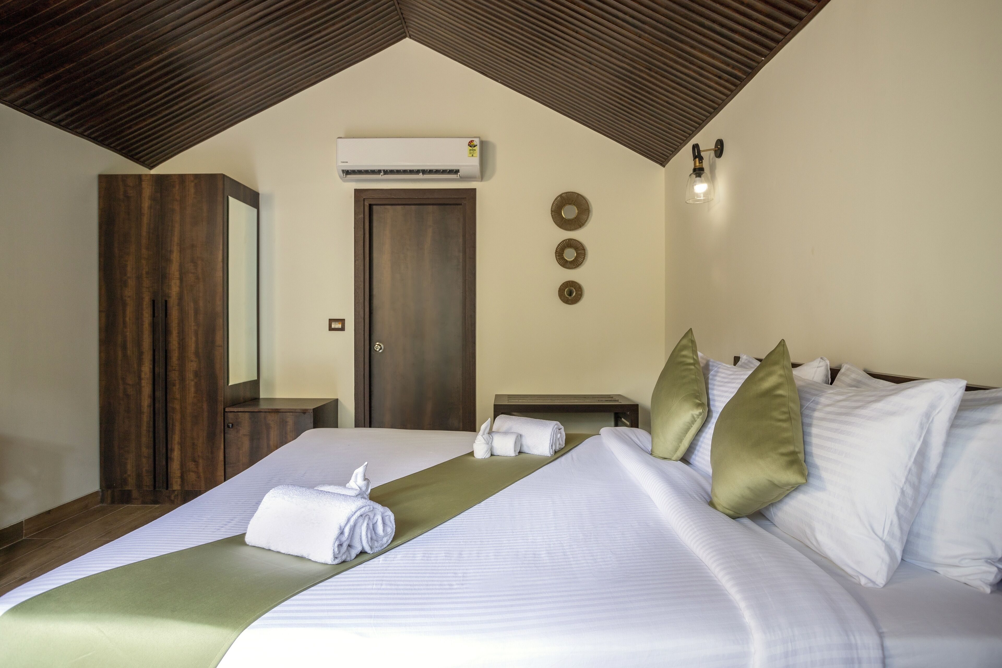 Quarto de hotel com cama grande, guarda-roupa de madeira, unidade de ar condicionado, espelho e luminária na parede.